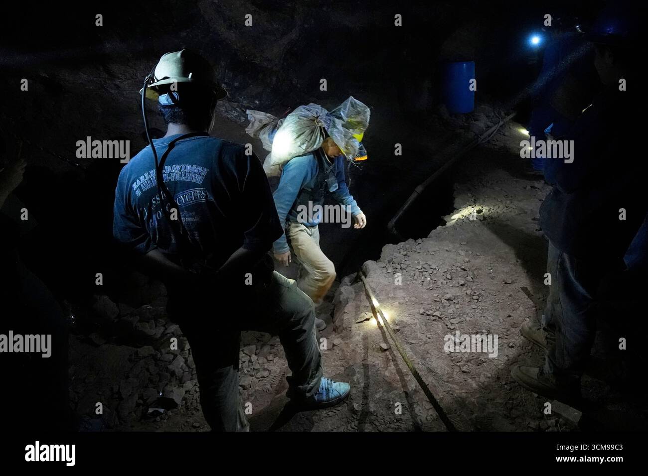 Miners carry sacks filled with mercury ore while their colleagues light ...