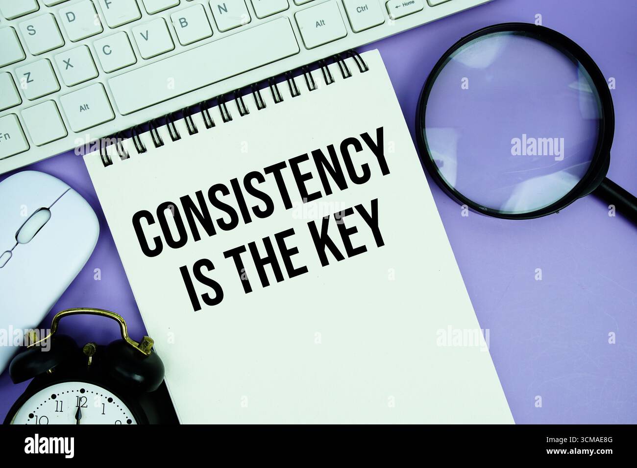 Notepad with the text "Consistency Is The Key" and white keyboard ...