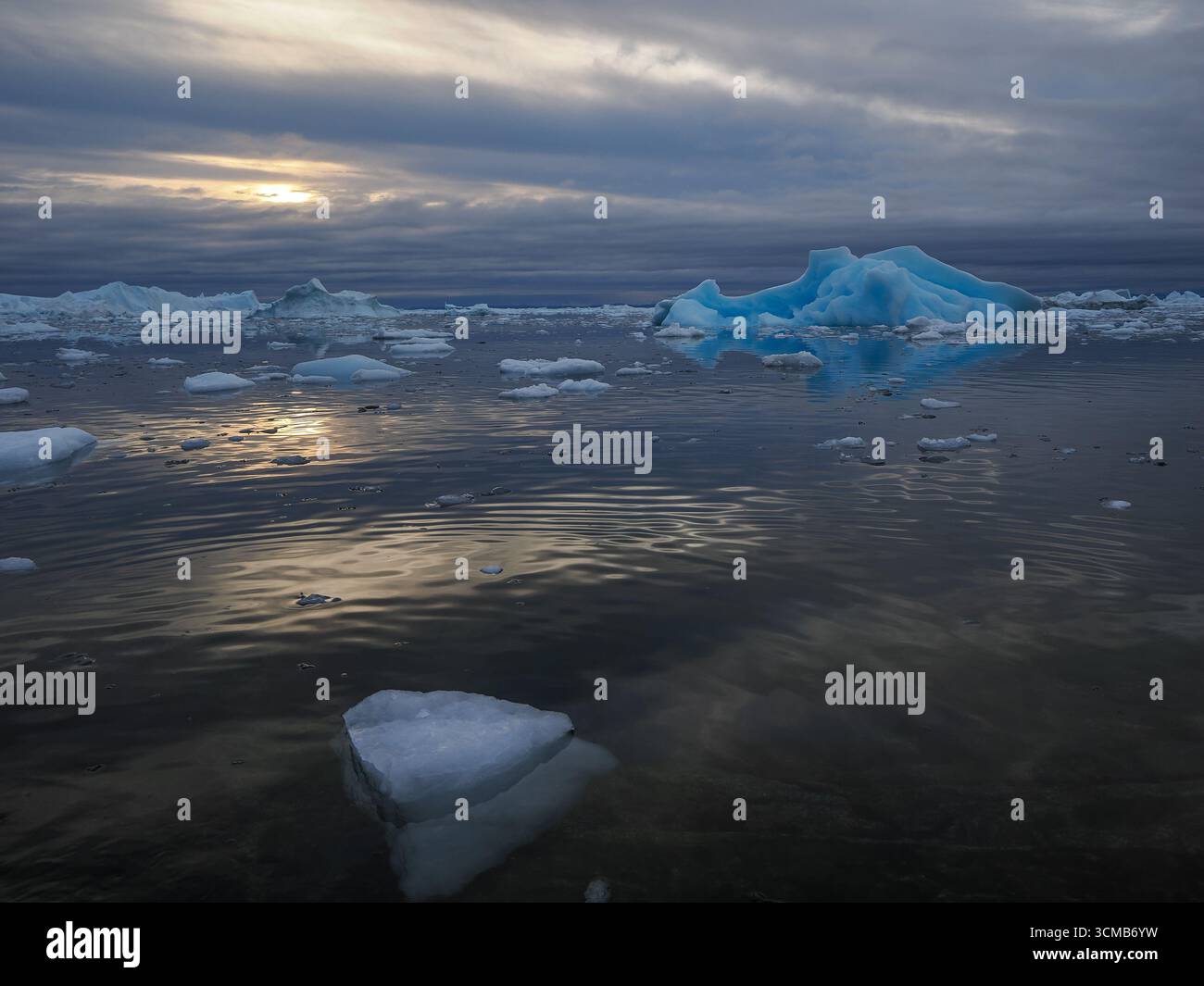 Scattered ice chunks and bright blue iceberg on calm arctic waters ...