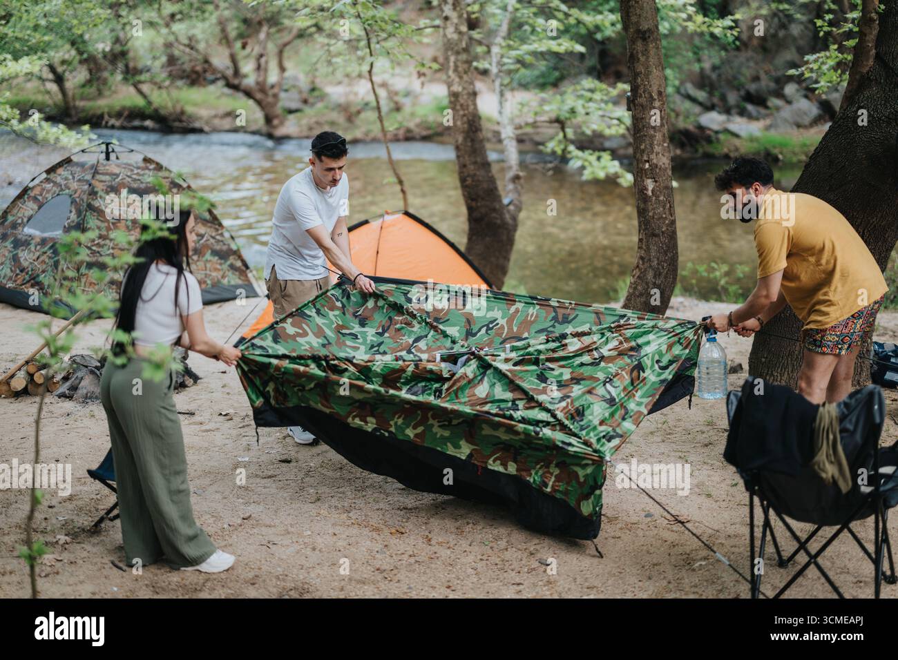 Group of friends setting up tents at scenic riverside campsite Stock ...
