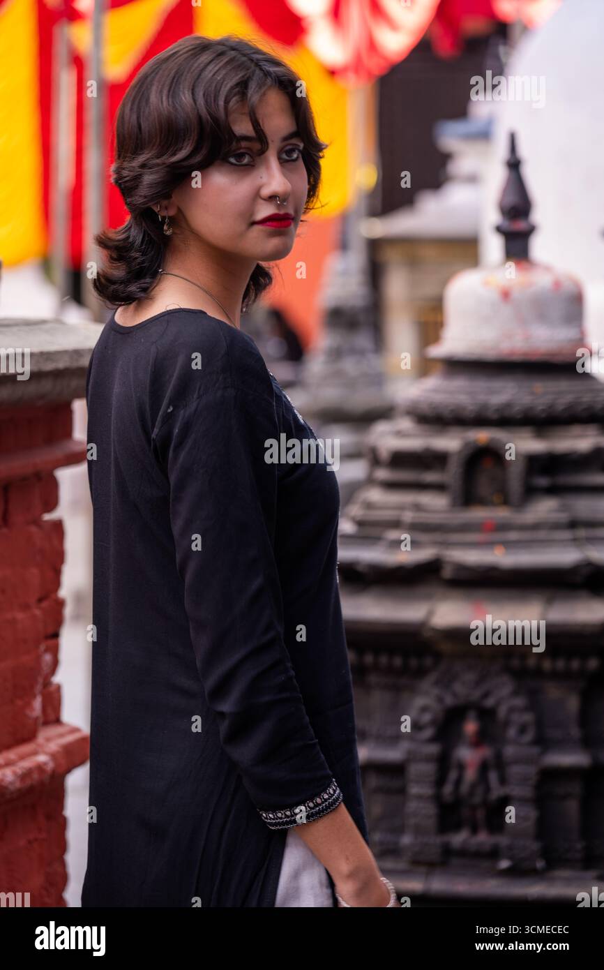 A young woman in a black dress with bold makeup poses near ancient ...