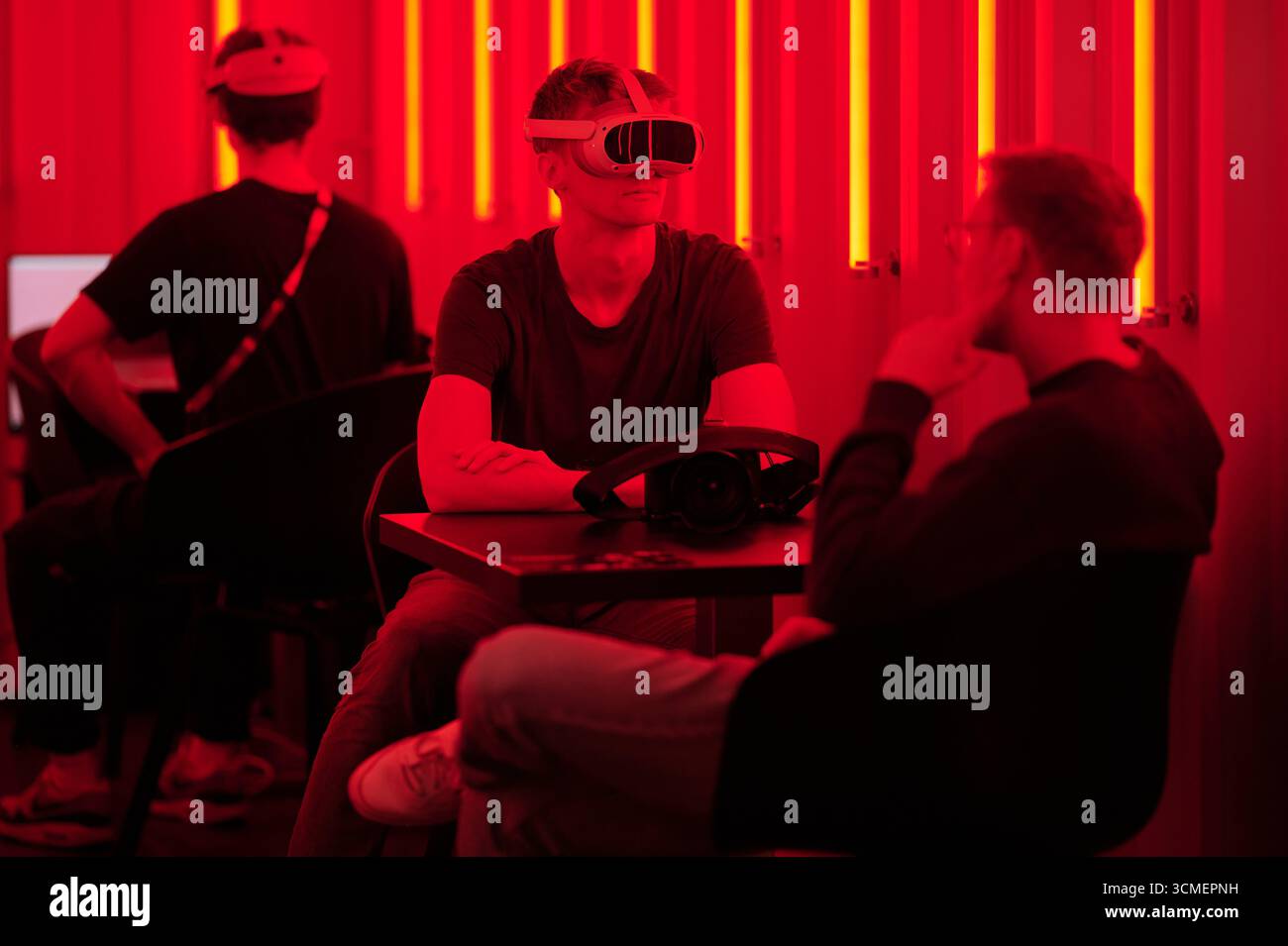Three men immersed in VR experience under vibrant red lights, seated ...