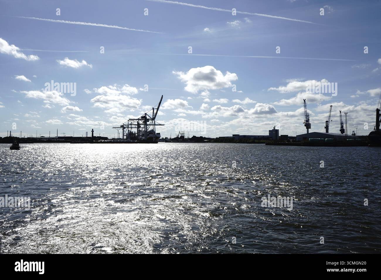 An industrial harbour with cranes and reflecting sunlight on the water ...