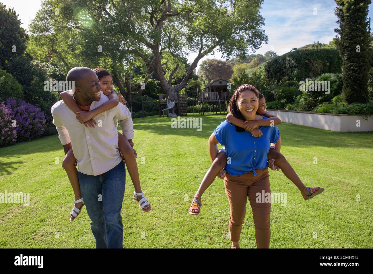 Diverse family walking in residential yard carrying children piggyback ...
