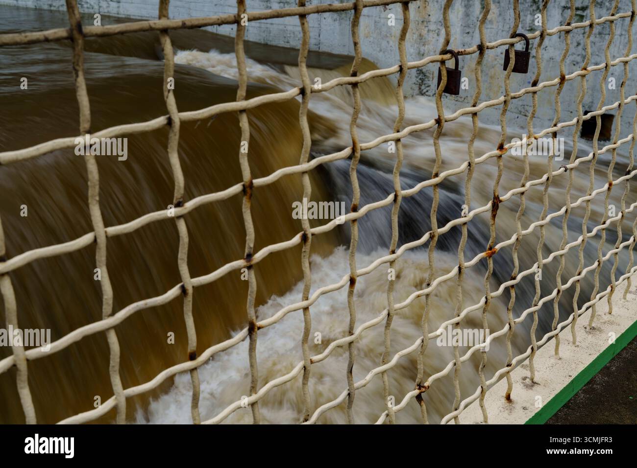 Powerful rushing water cascades down a dam, seen through tight safety ...
