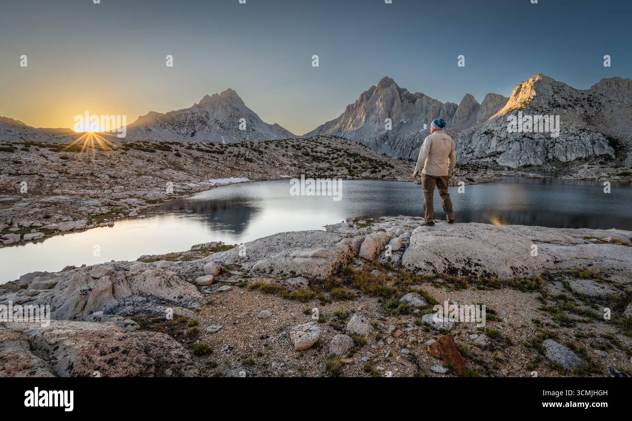Rear view of a man standing on a rock in front of Grinnell lake at dawn ...