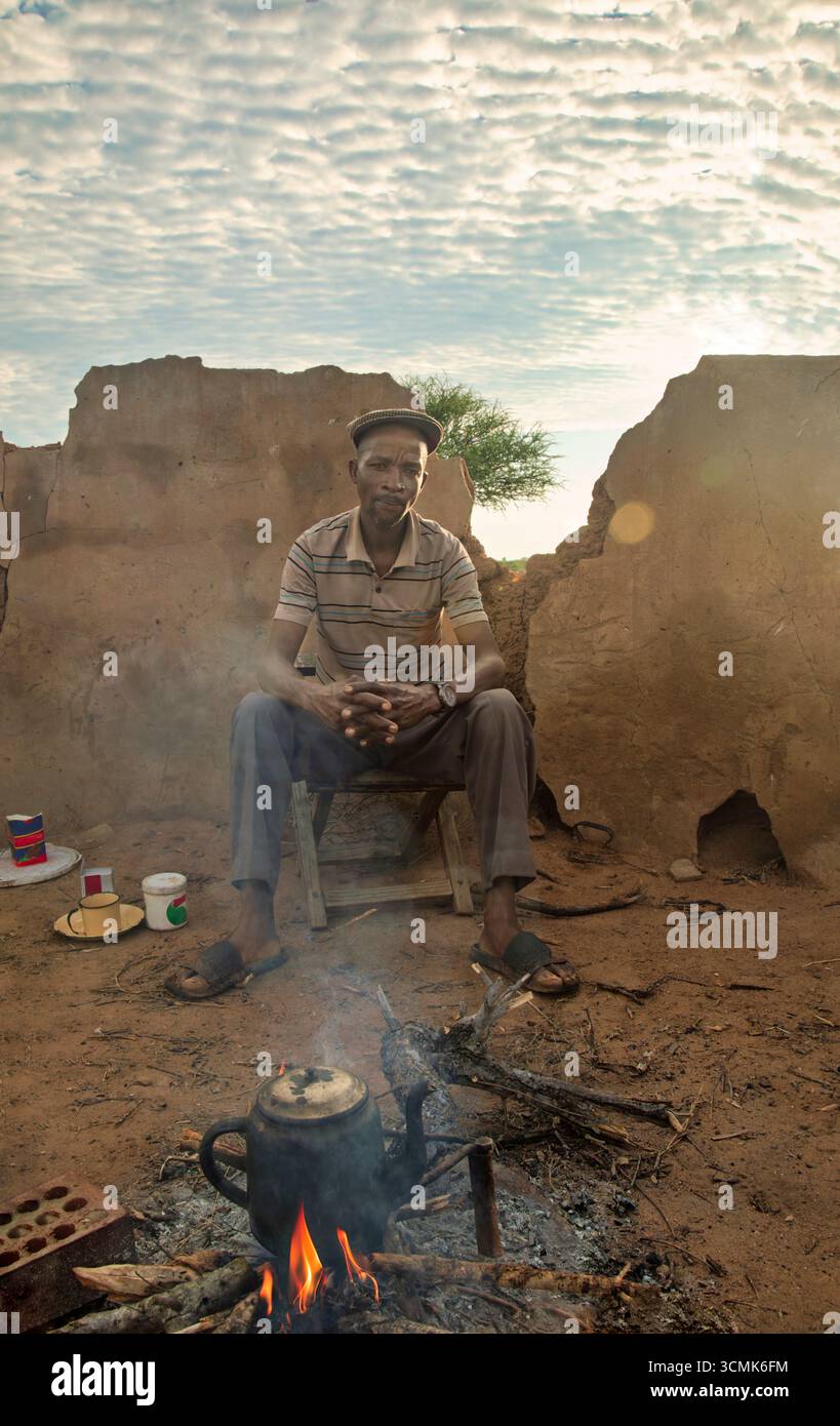 village african man cooking on open fire in the yard at sunset, waiting ...