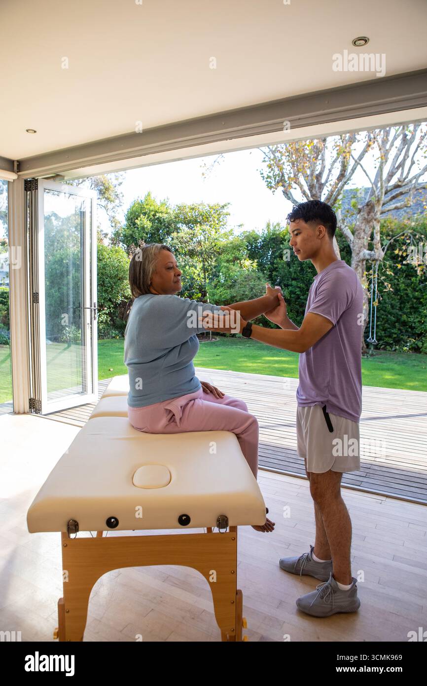 Diverse therapist and patient performing seated arm stretch on therapy ...