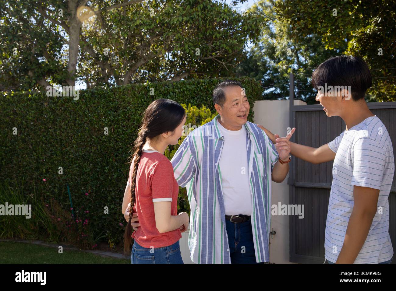 Asian family talking in suburban garden on grass lawn next to trimmed ...