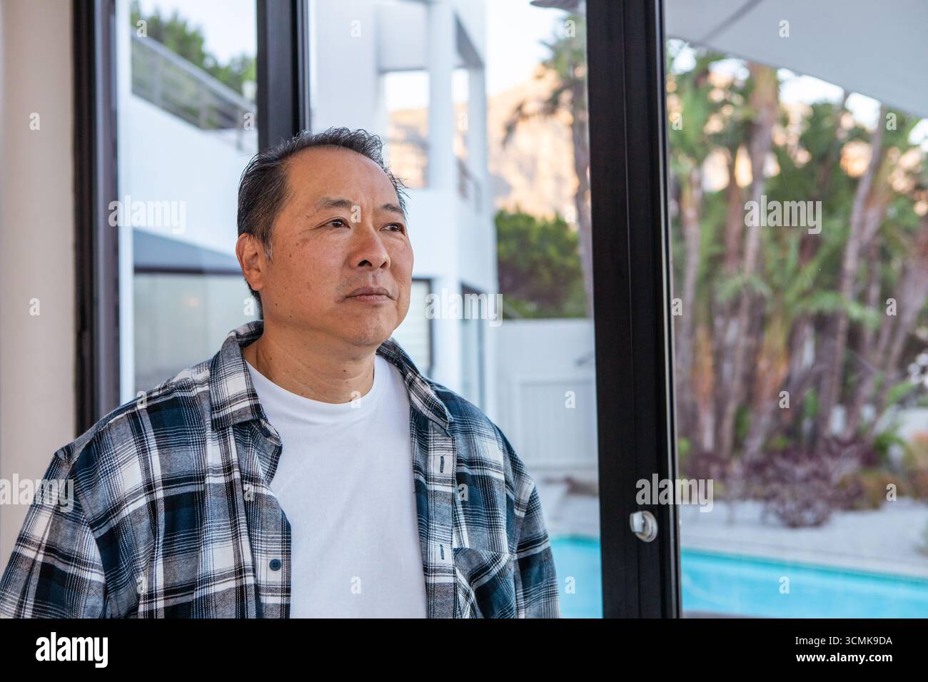 Asian man standing inside modern home near sliding door overlooking ...