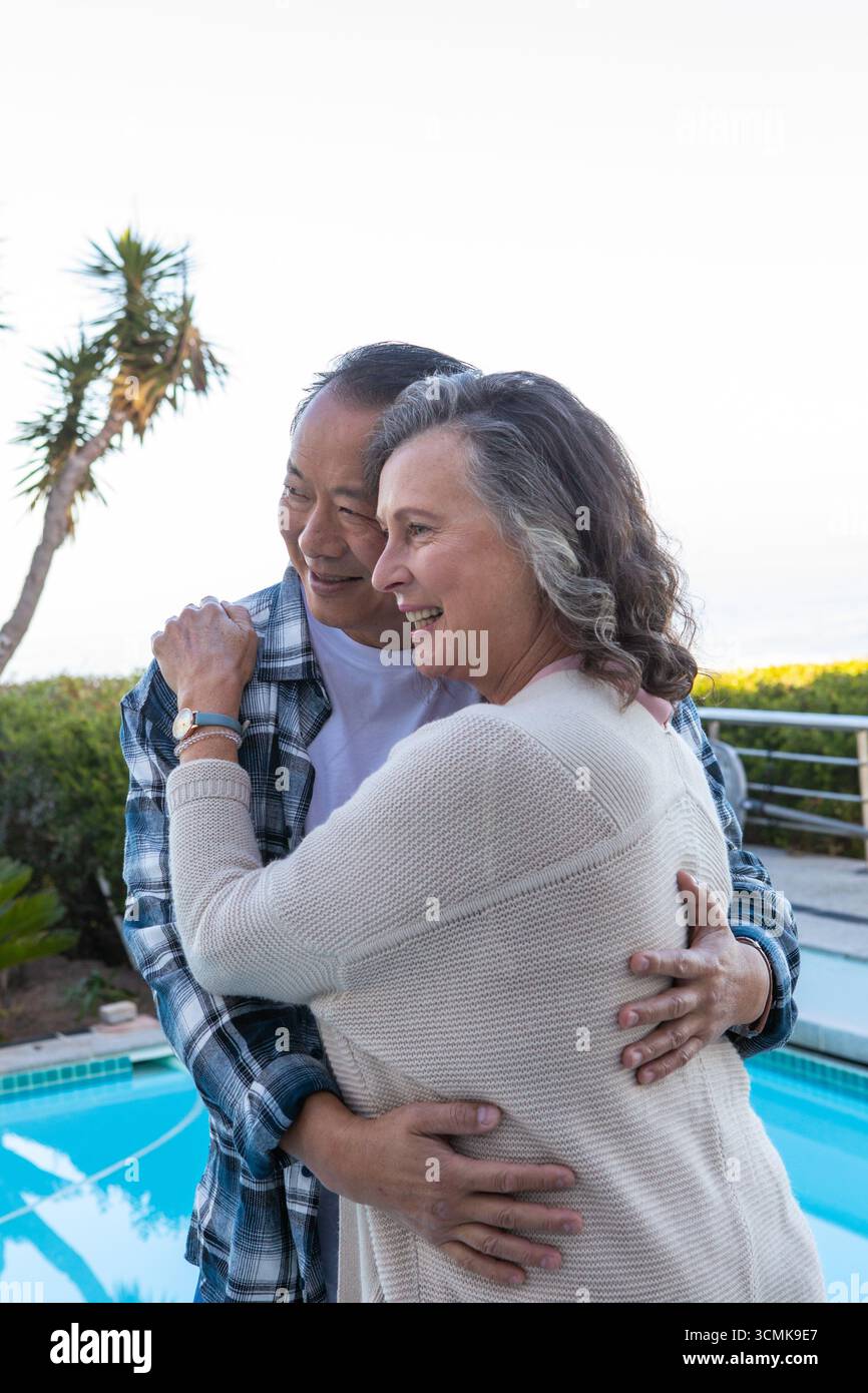 Asian couple hugging at edge of turquoise pool showing wristwatch by ...