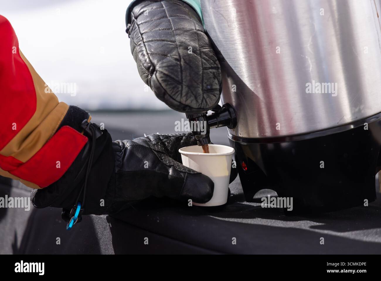 Gloved hands pouring a hot beverage from a thermos into a paper cup on ...