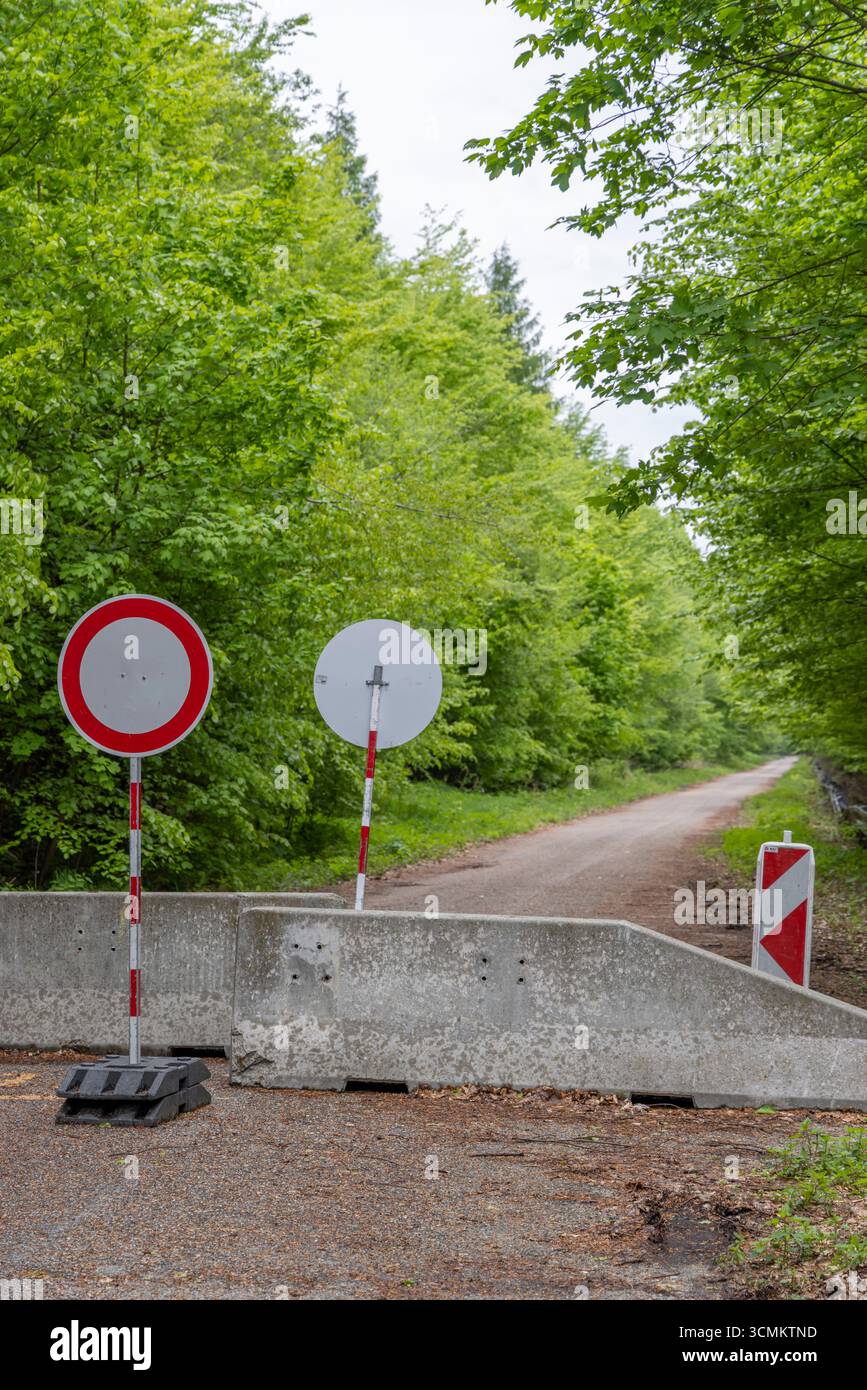 Concrete roadblock and traffic signs blocking access to a forest road ...