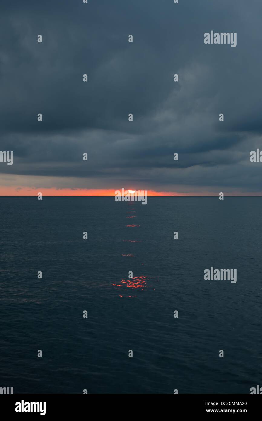 Red sunrise setting over sea under heavy, dark clouds. Moody and ...