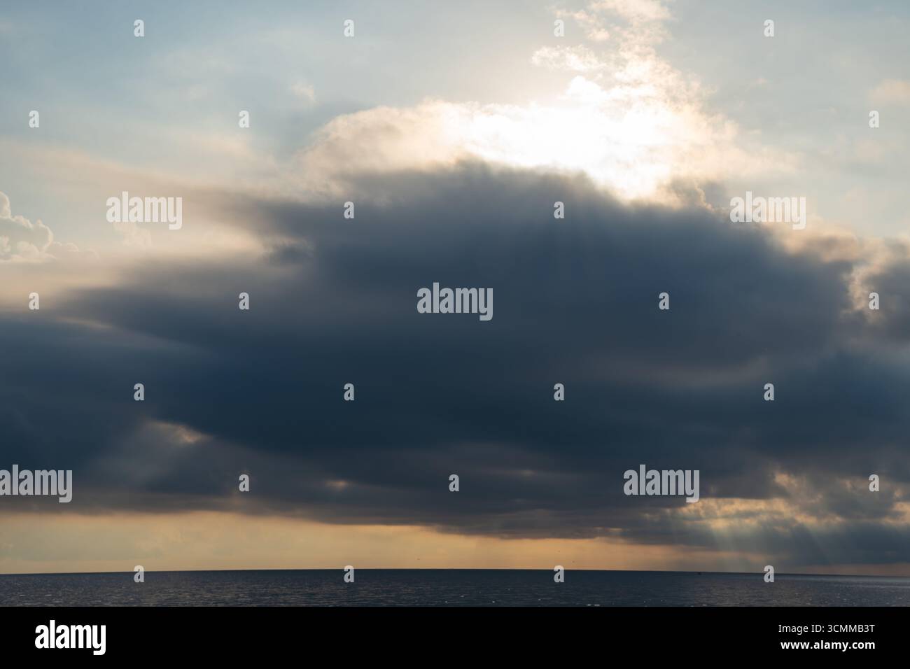 Sun rays breaking through large, dark cloud over calm ocean. Straight ...