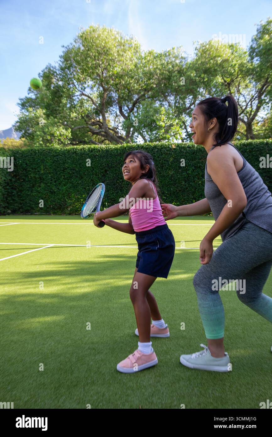 Asian mother and daughter practicing tennis swing on grass court with ...