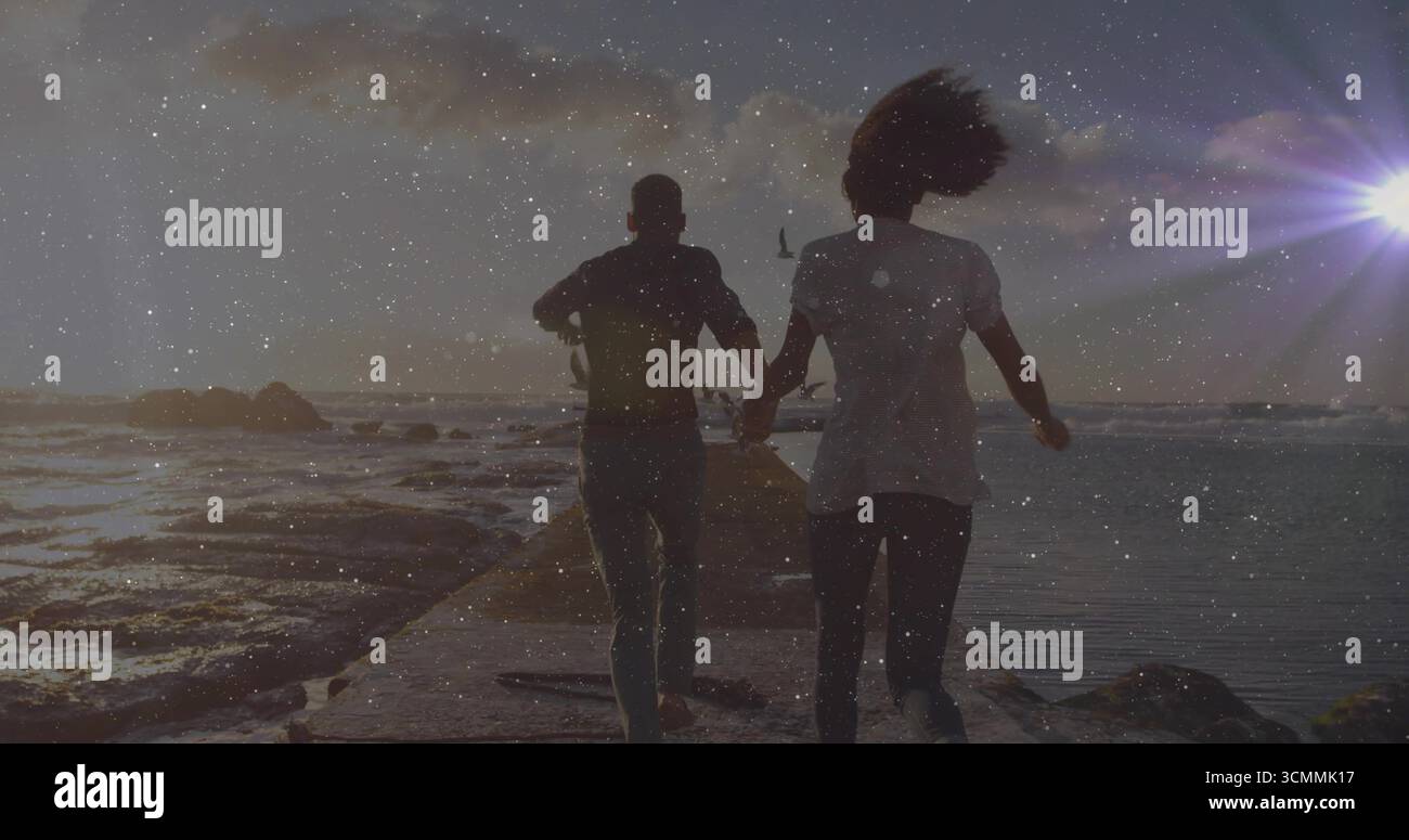 Running couple holding hands along concrete jetty at sunset, crashing ...