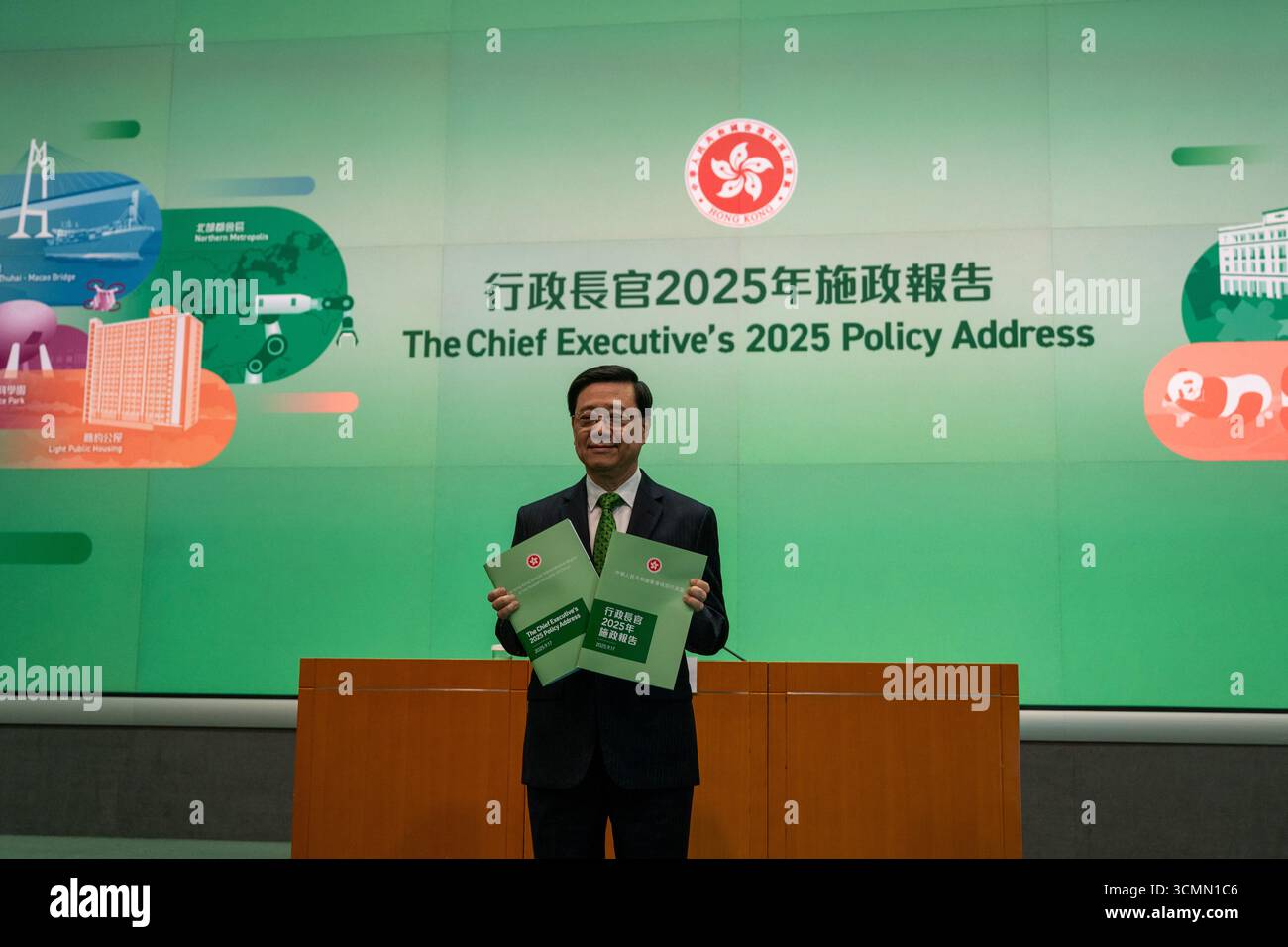 Hong Kong Chief Executive John Lee holding up two booklets of his 2025 Policy Address while ...