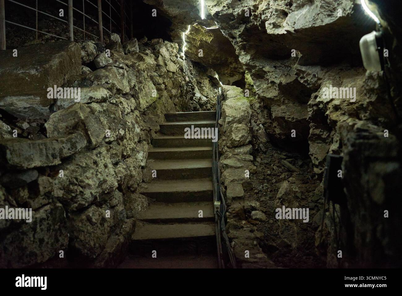 Stone steps leading upward through narrow rocky cave passageway, rough ...