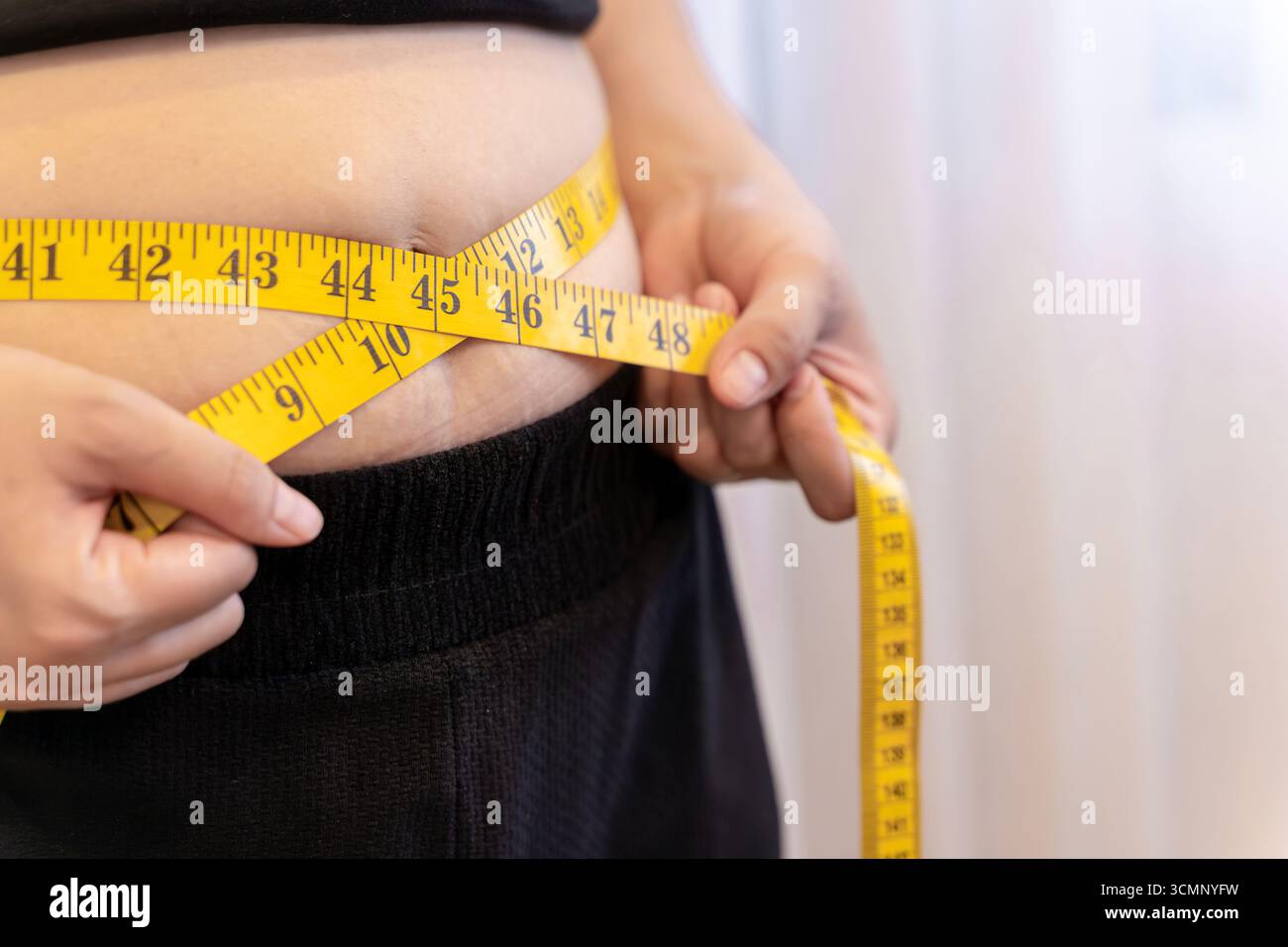 Asian woman using a tape measure around her waist to check body size ...