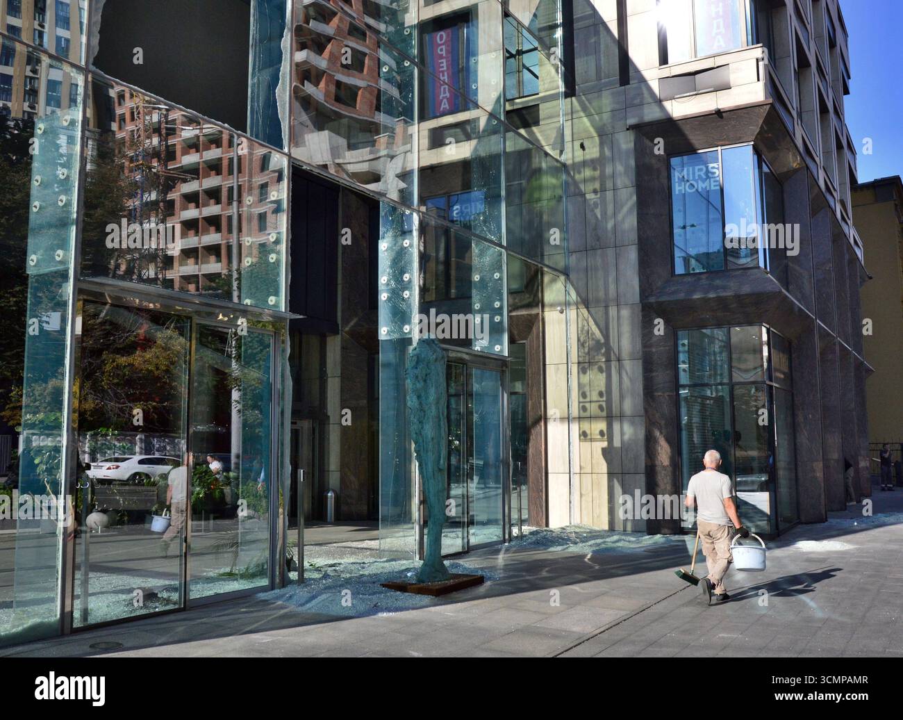 Men walk past a pile of glass facade panels from a building, shattered during a combined Russian ...