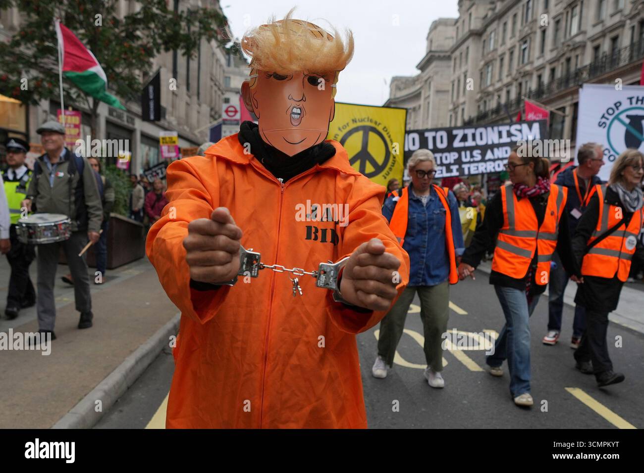 A protester wearing a jail outfit and wearing a Trump mask walks ahead ...