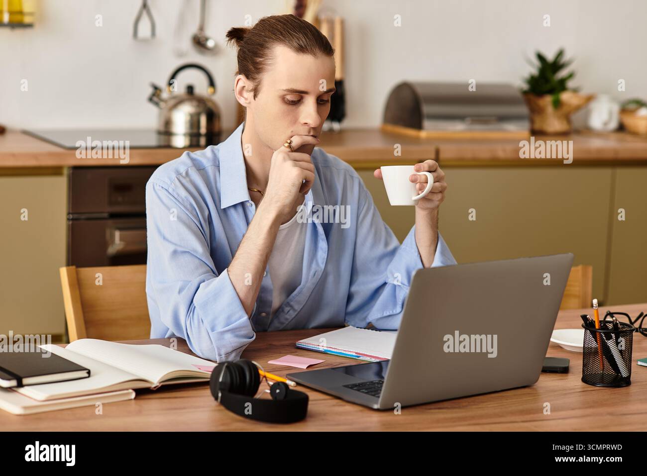 A young handsome man reflects on his work while sipping coffee at a ...