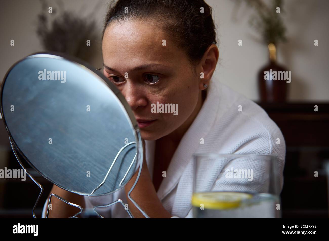 A concentrated woman applies makeup using a mirror, capturing a moment ...
