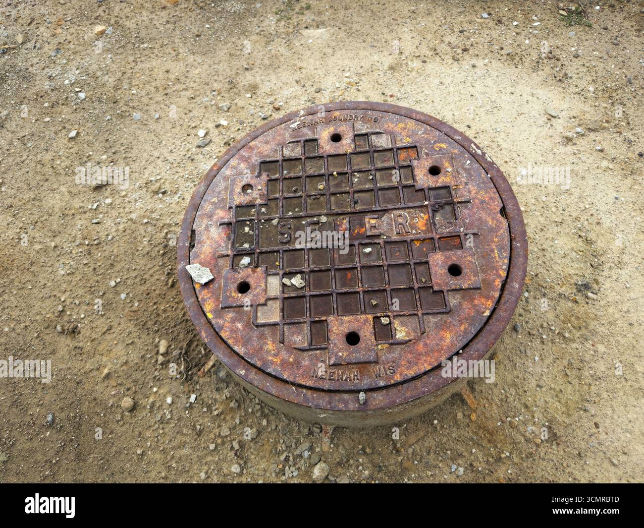 An old, rusty manhole cover protrudes out of excavated ground as part ...