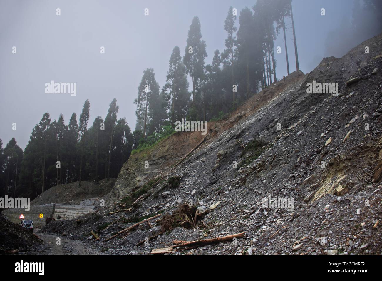 Landslide disrupting a mountain slope road, surrounded by misty forest ...