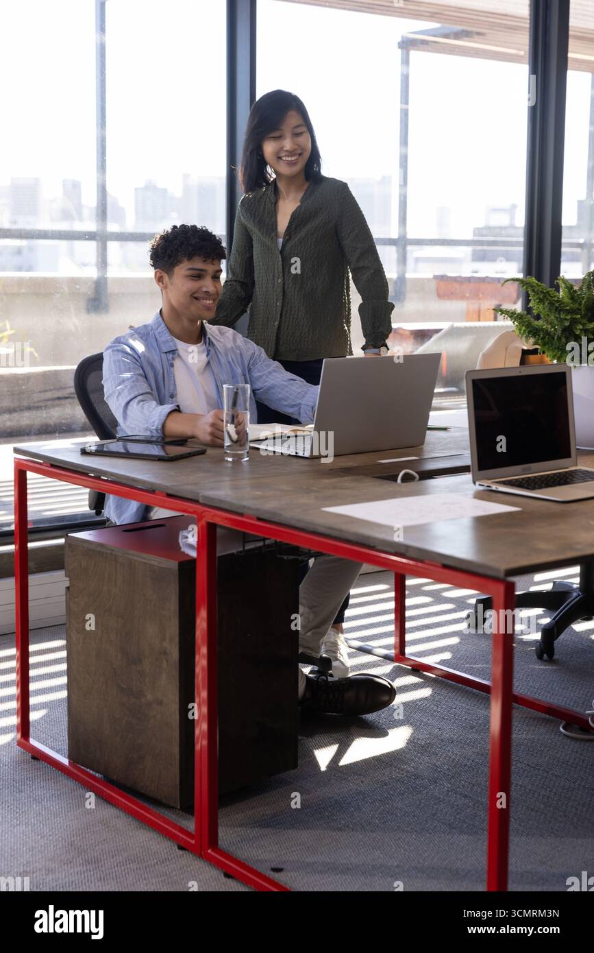 Diverse coworkers collaborating at office table using two laptops ...