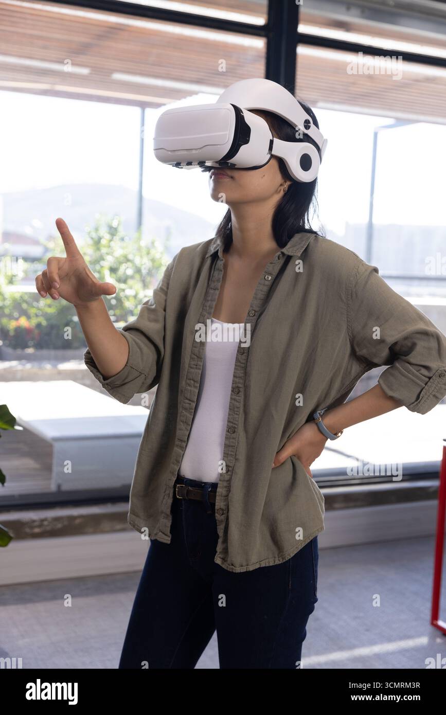 Asian woman wearing white vr headset and reaching forward in office ...