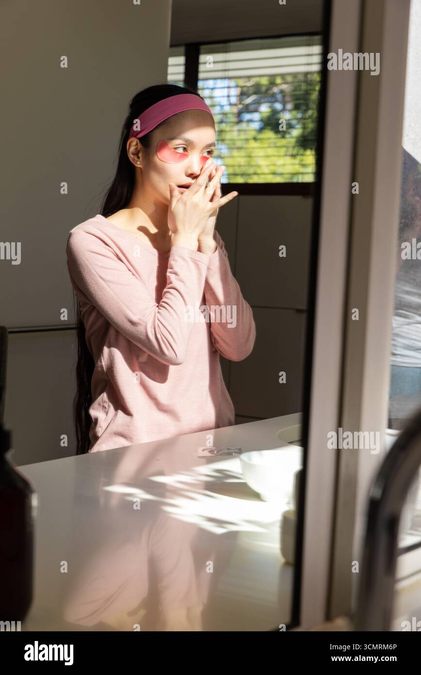 Asian woman wearing pink headband touching face with under-eye gel ...