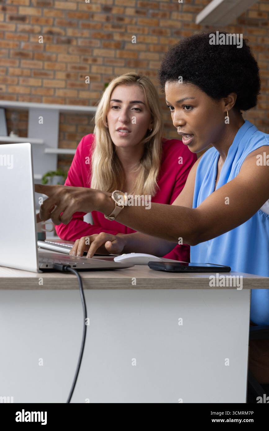 Diverse female coworkers in business attire pointing at laptop typing ...