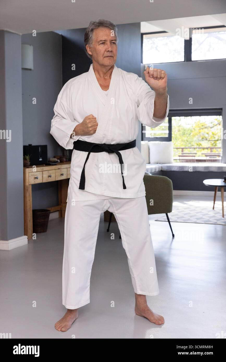 Senior male practicing forward punch in living room by windows wearing ...