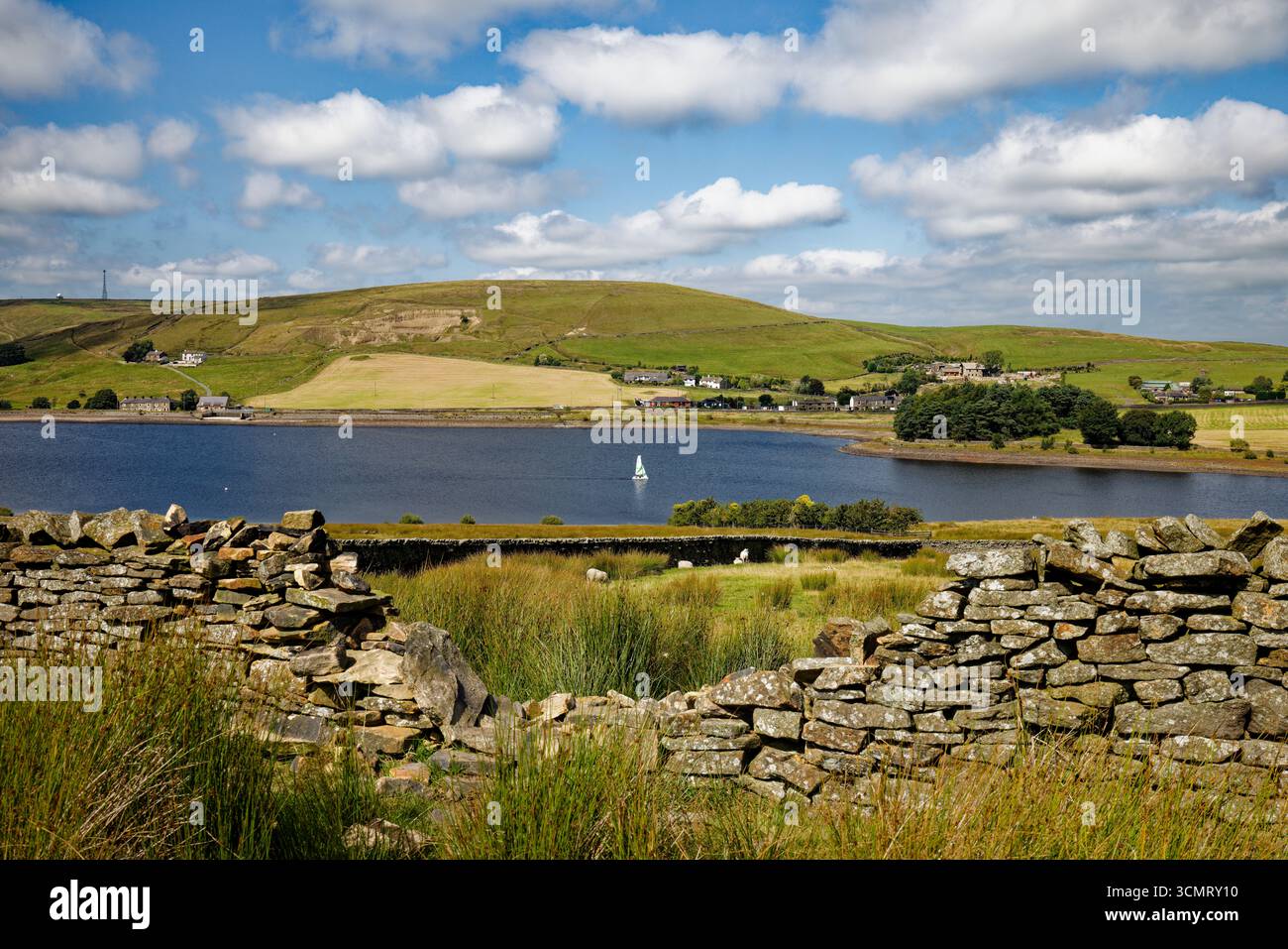 A gap in a drystone wall frames a view of Clowbridge Reservoir with a ...