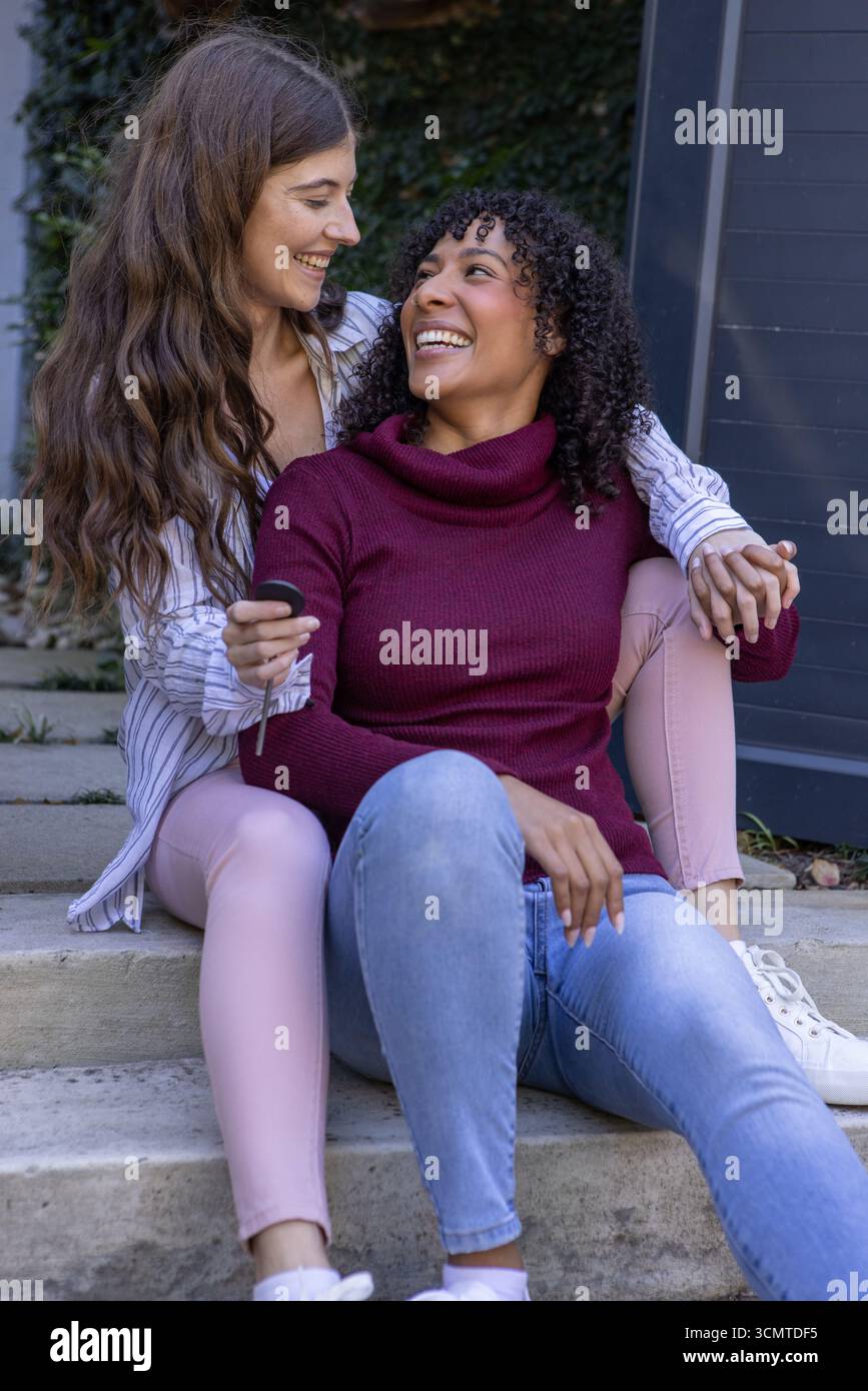 Diverse women hugging on outside concrete steps at residence with car ...