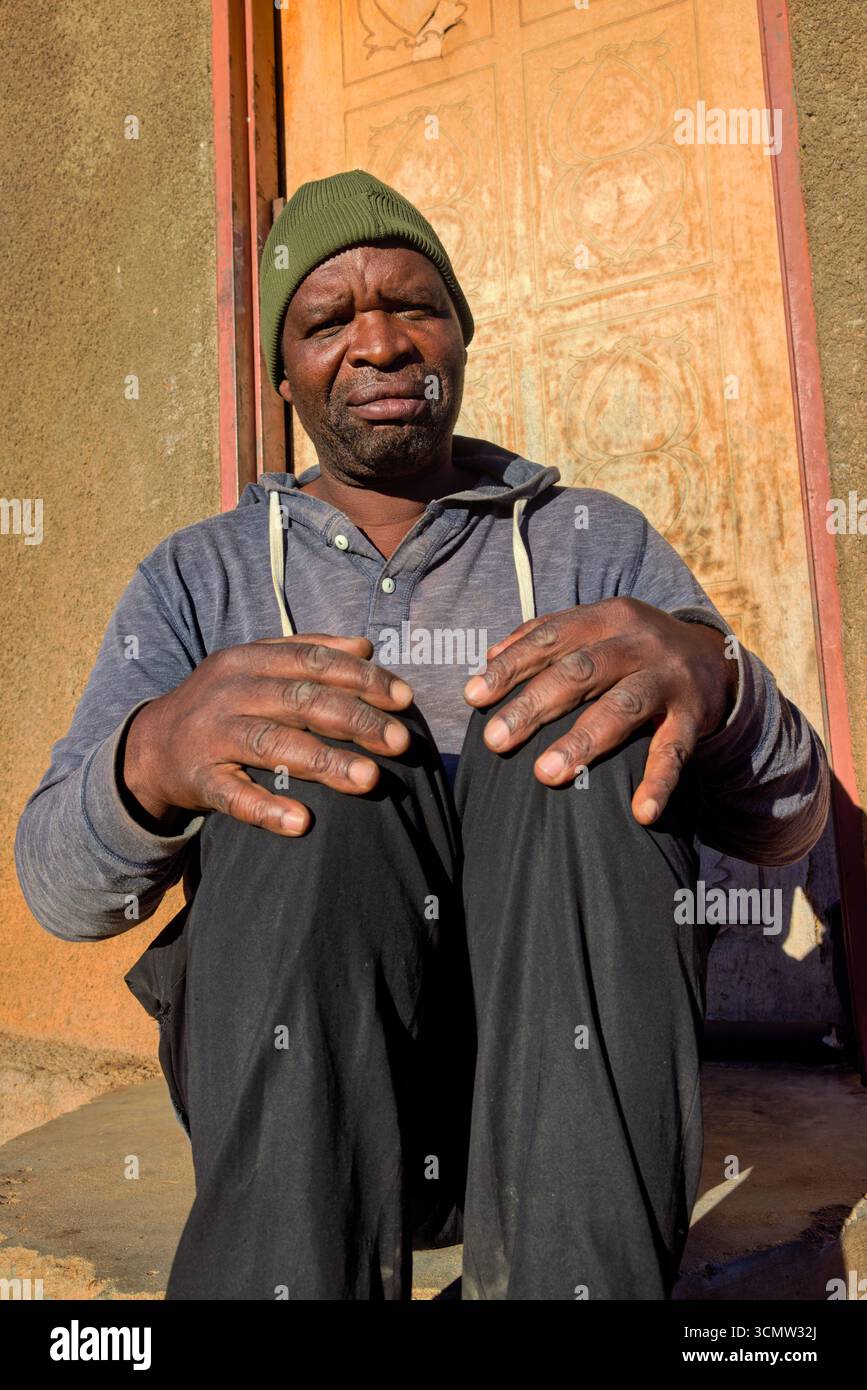 village single african man sited in front of the house in the yard ...