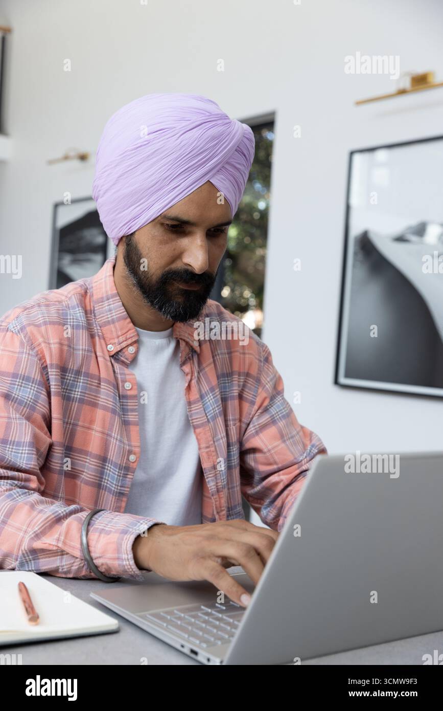 Indian man wearing turban typing on silver laptop keyboard at house ...