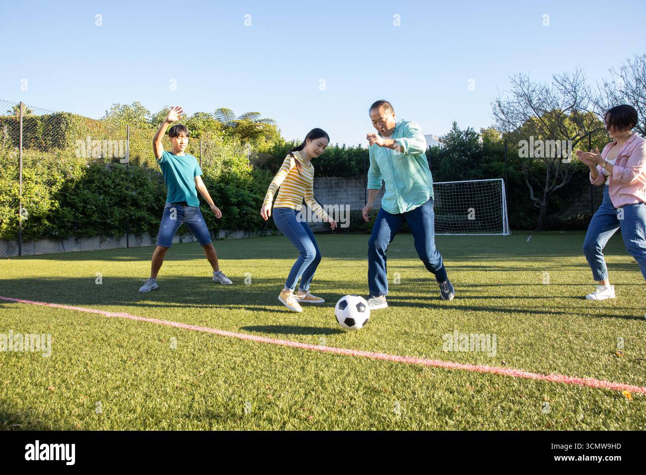 Diverse family playing soccer on backyard grass field next to small ...