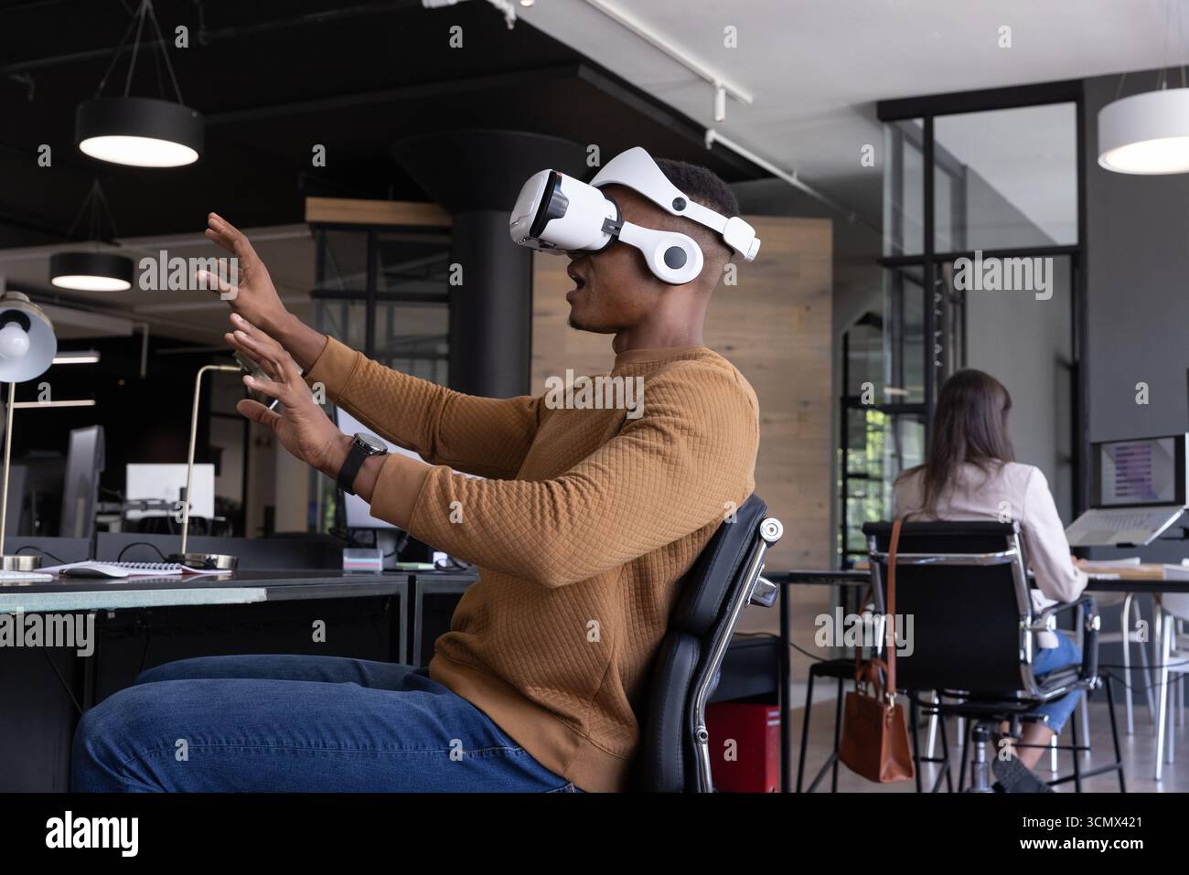 Employee wearing vr headset extending arms at open-plan desk with ...