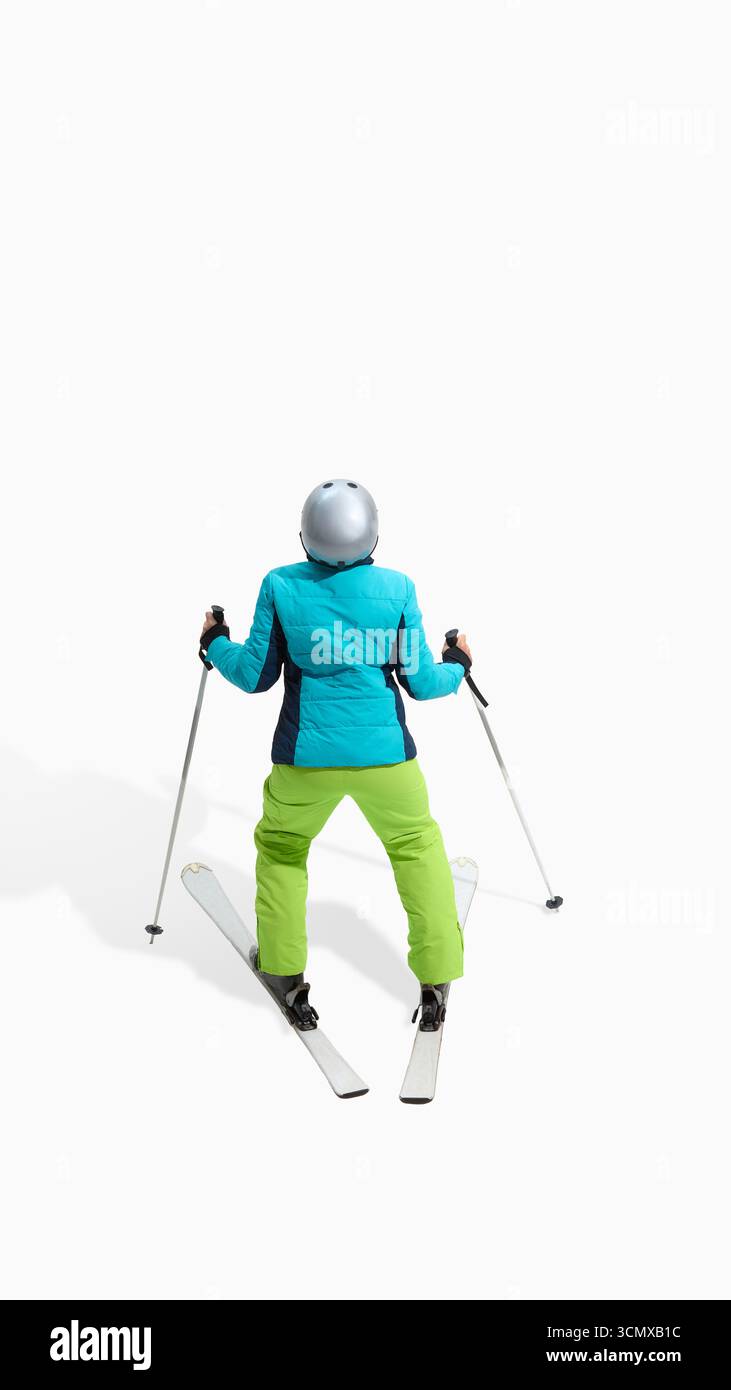 Female skier seen from back standing in relaxed position with ski poles ...