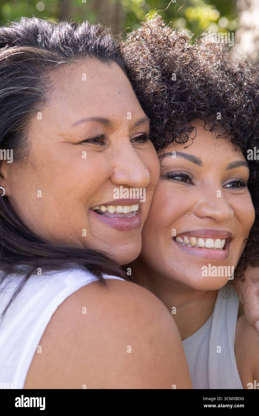 Senior mother and daughter pressing faces together outdoors in sunlit ...