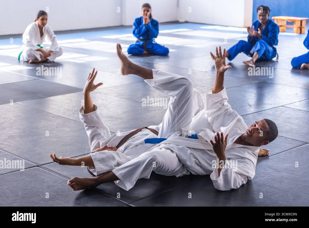 Diverse martial arts students performing ground throw on mat in ...