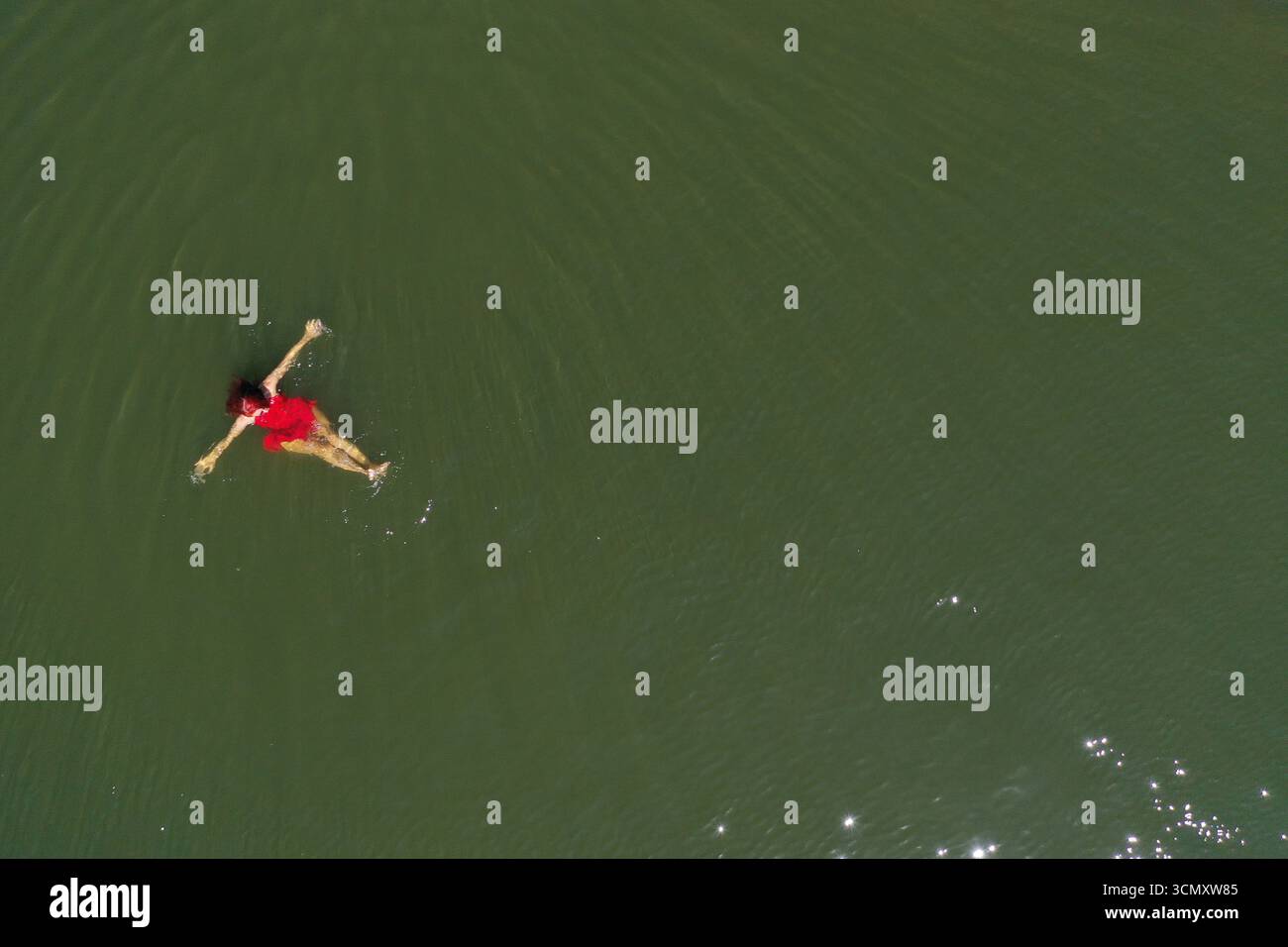 Aerial view of gorgeous woman in red dress floating on calm water by ...