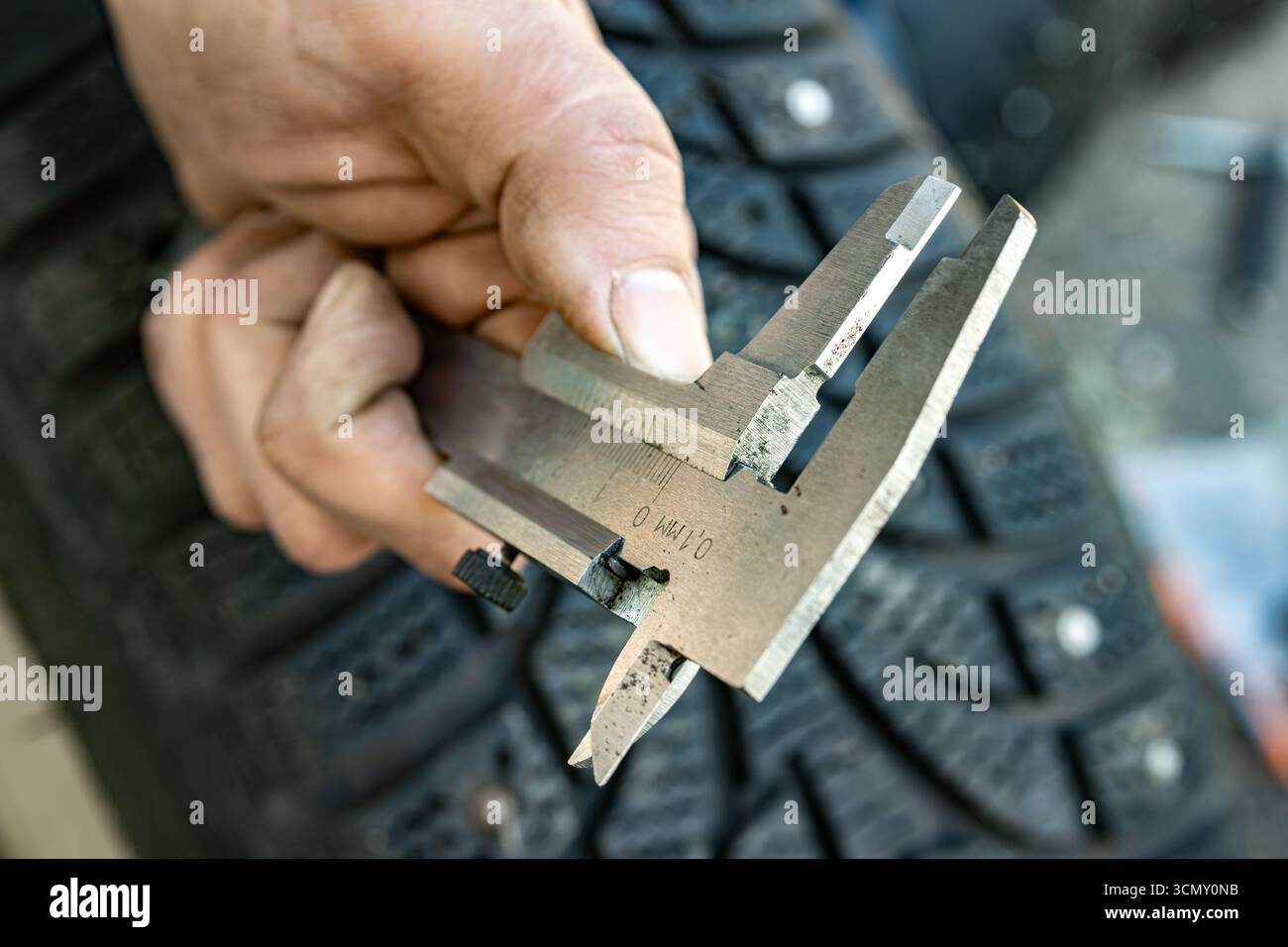 Close-up of a metal vernier caliper in hand, positioned above a studded ...