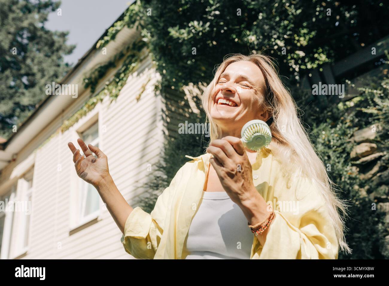 Happy laughing Caucasian woman uses portable fan in summer on July ...