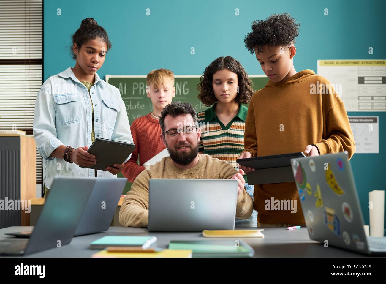 Caucasian man teaching diverse group of teenagers using digital tablets ...
