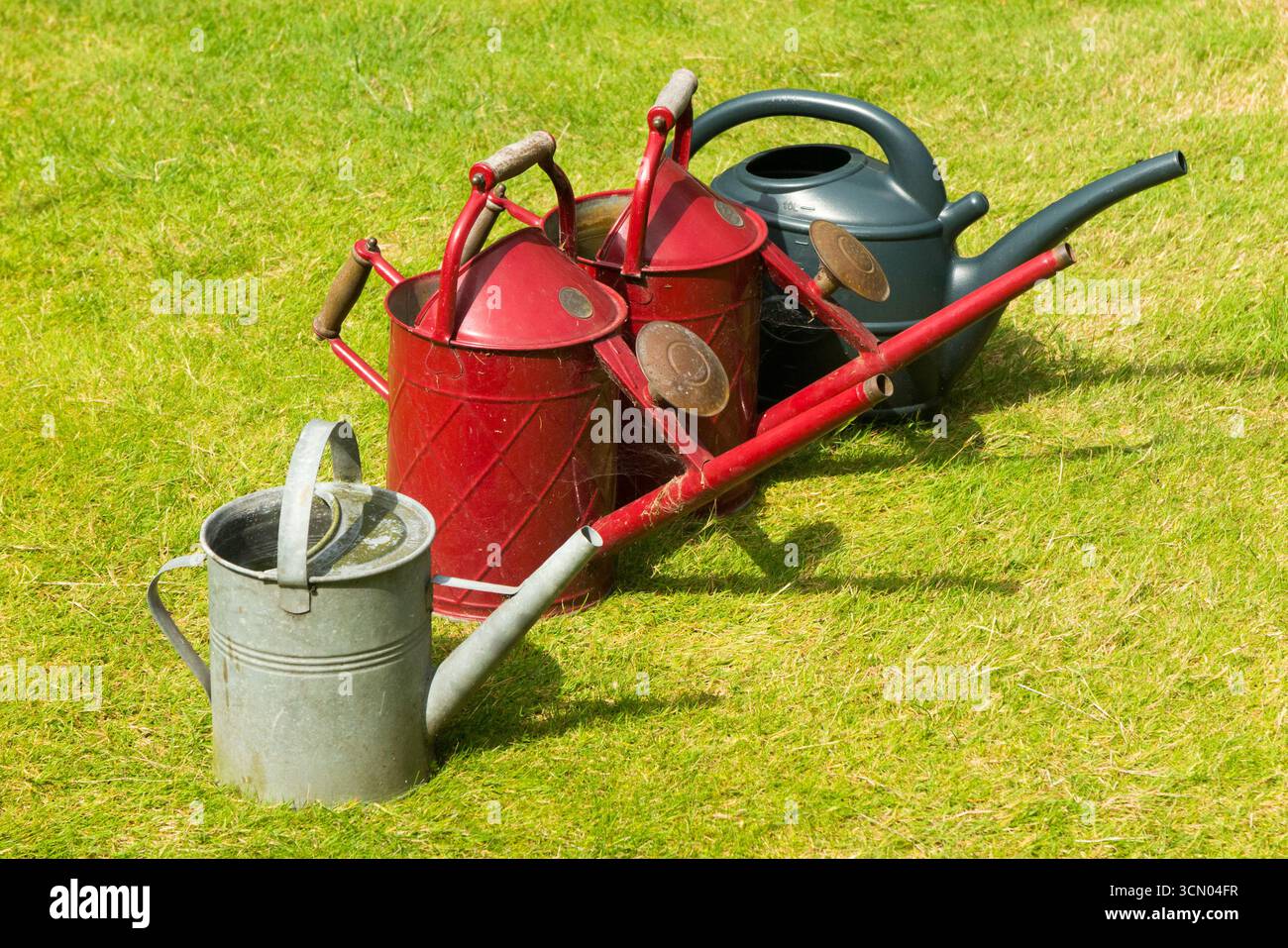 Watering cans, some with water, in a line arrangement on a green grass ...