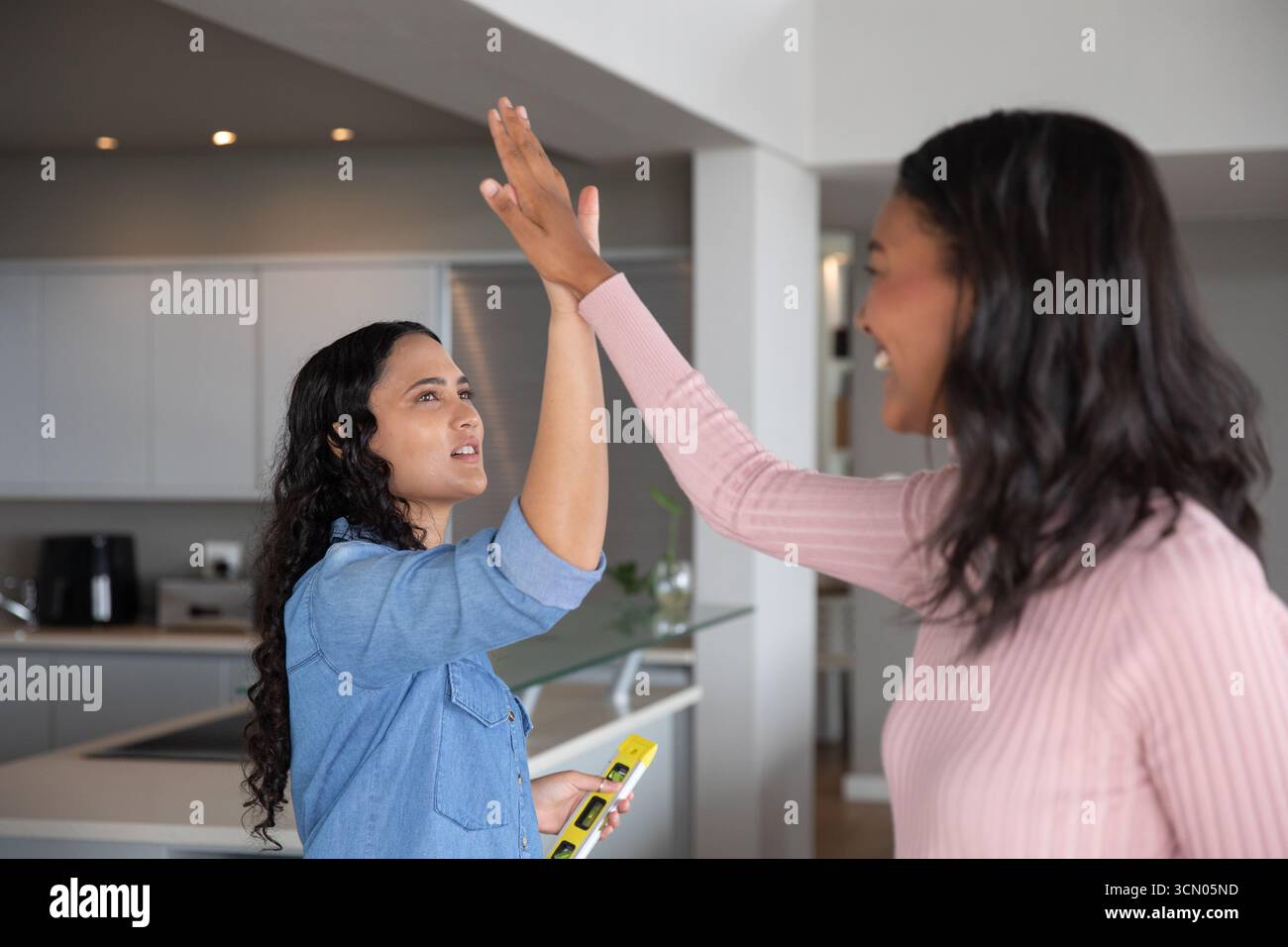 Diverse female friends giving high-five while using spirit level by ...